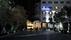 Hotel com entrada bem iluminada, área de piscina e um edifício com várias janelas.