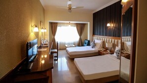 Quarto de hotel com duas camas, uma escrivaninha, uma cadeira, uma televisão e um ventilador de teto.