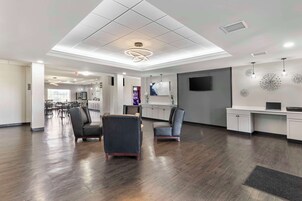 Um hall amplo com design moderno, apresentando uma grande área de estar com poltronas de couro, uma cozinha com bancada e eletrodomésticos, e uma TV de tela plana na parede.