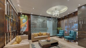 Uma sala de estar moderna com um sofá bege, duas poltronas verde-água, uma mesa de centro e um lustre.