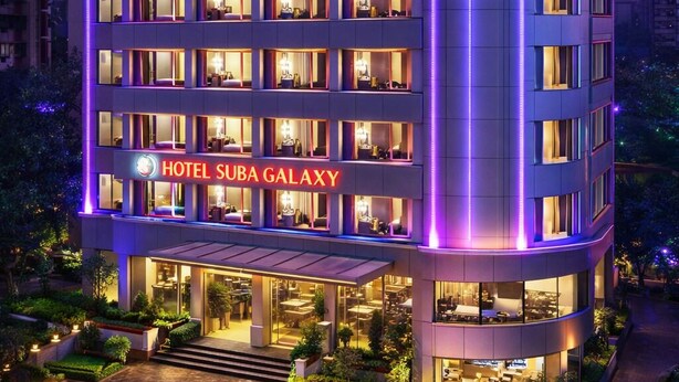 Um hotel de vários andares com um grande letreiro 'HOTEL SUBA GALAXY', apresentando um design moderno com varandas e uma entrada bem iluminada.