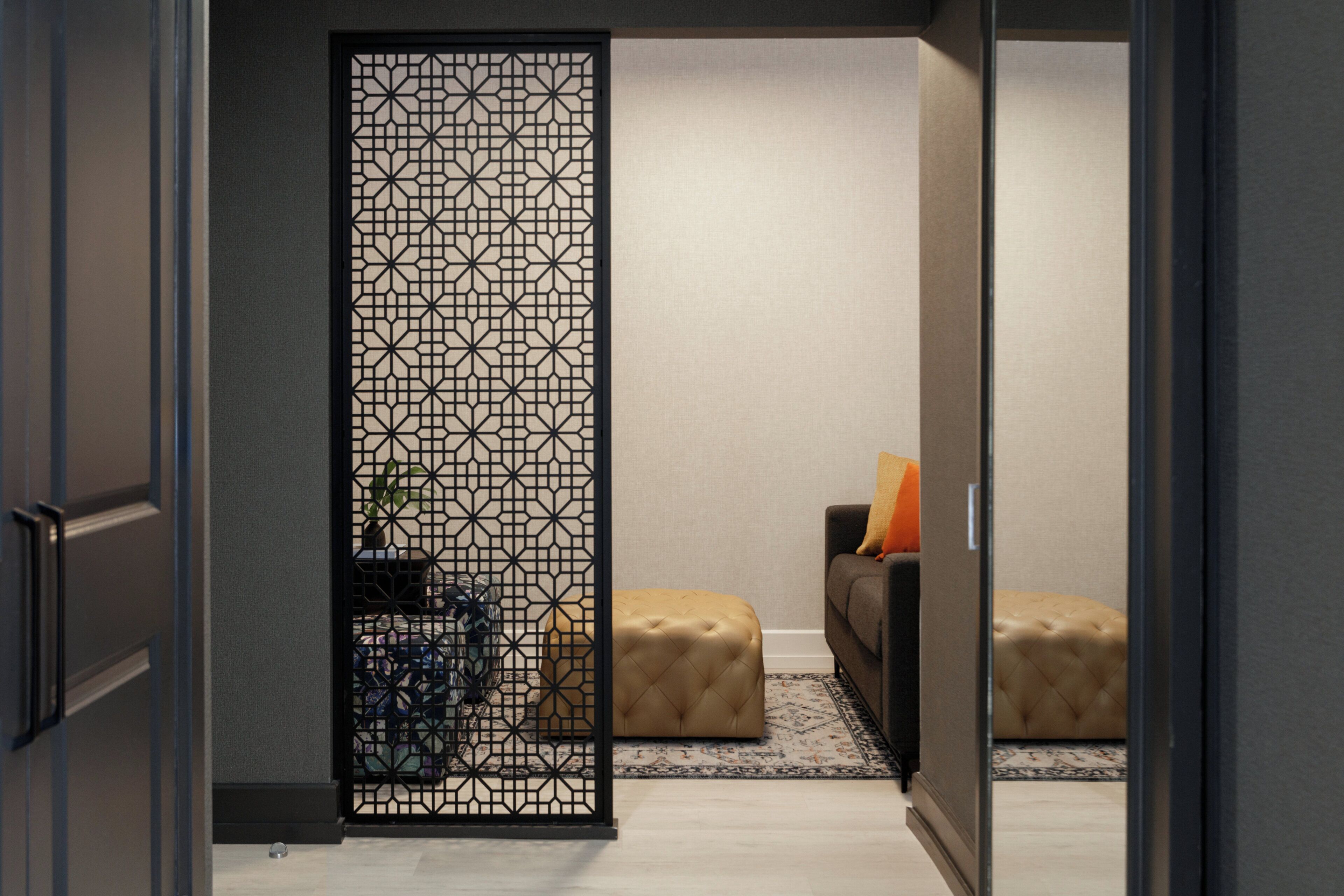 Quarto com porta deslizante, sofá, banquinho e divisória estampada.
