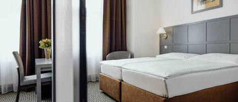 Quarto de hotel com cama, escrivaninha, cadeira e janela com cortinas.