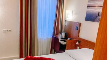Quarto de hotel com cama, escrivaninha, cadeira, cafeteira e um quadro na parede.