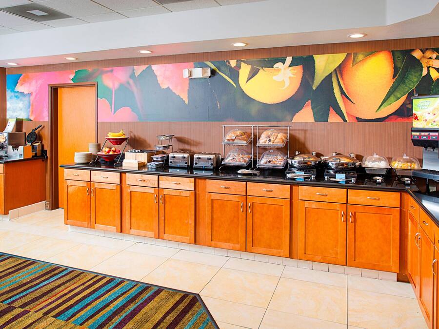 Espaço de café da manhã de hotel com serviço de buffet, armários de madeira e um mural colorido na parede.