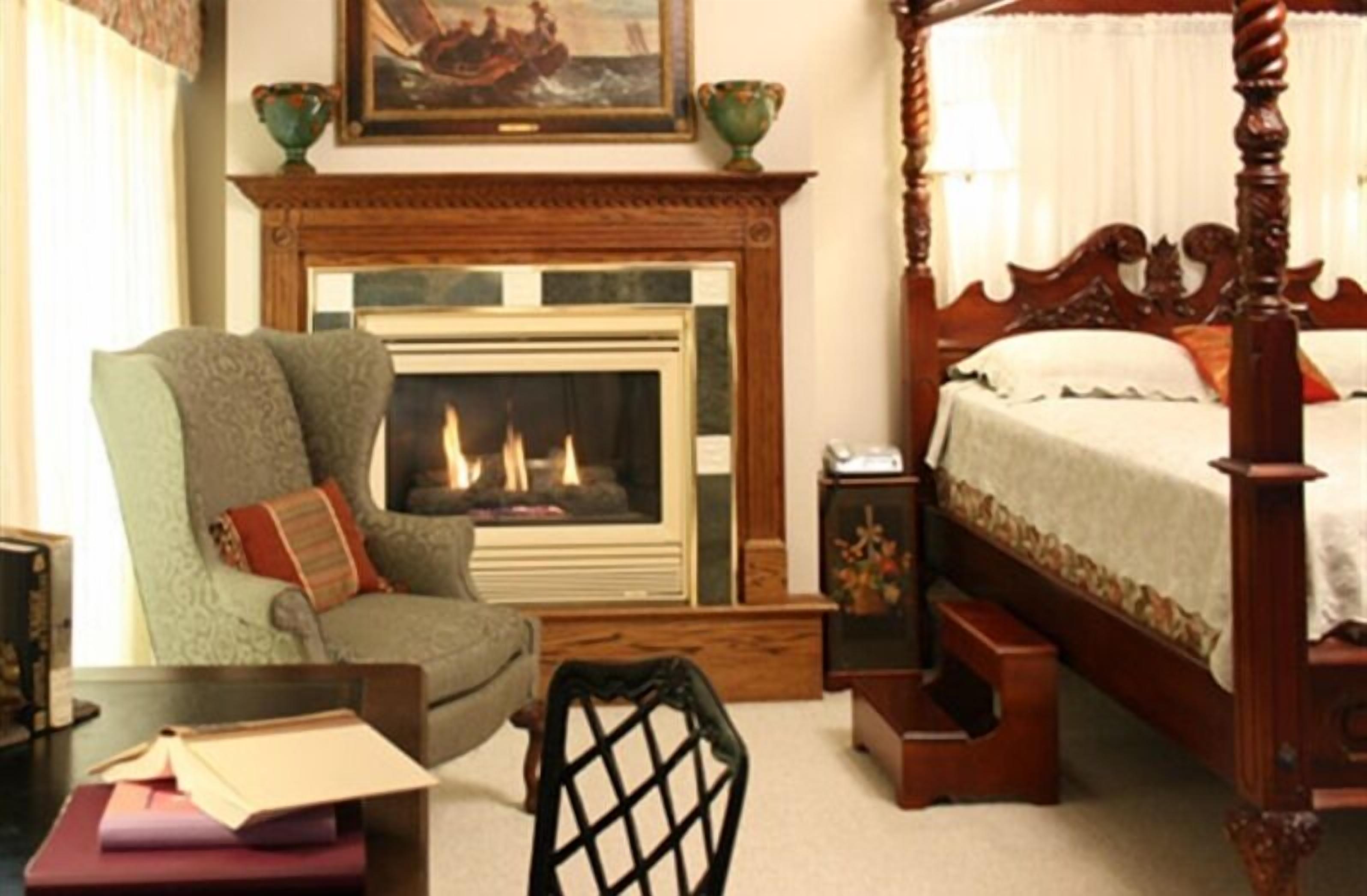 Um quarto com cama de dossel, lareira, poltrona verde e uma cadeira de madeira.