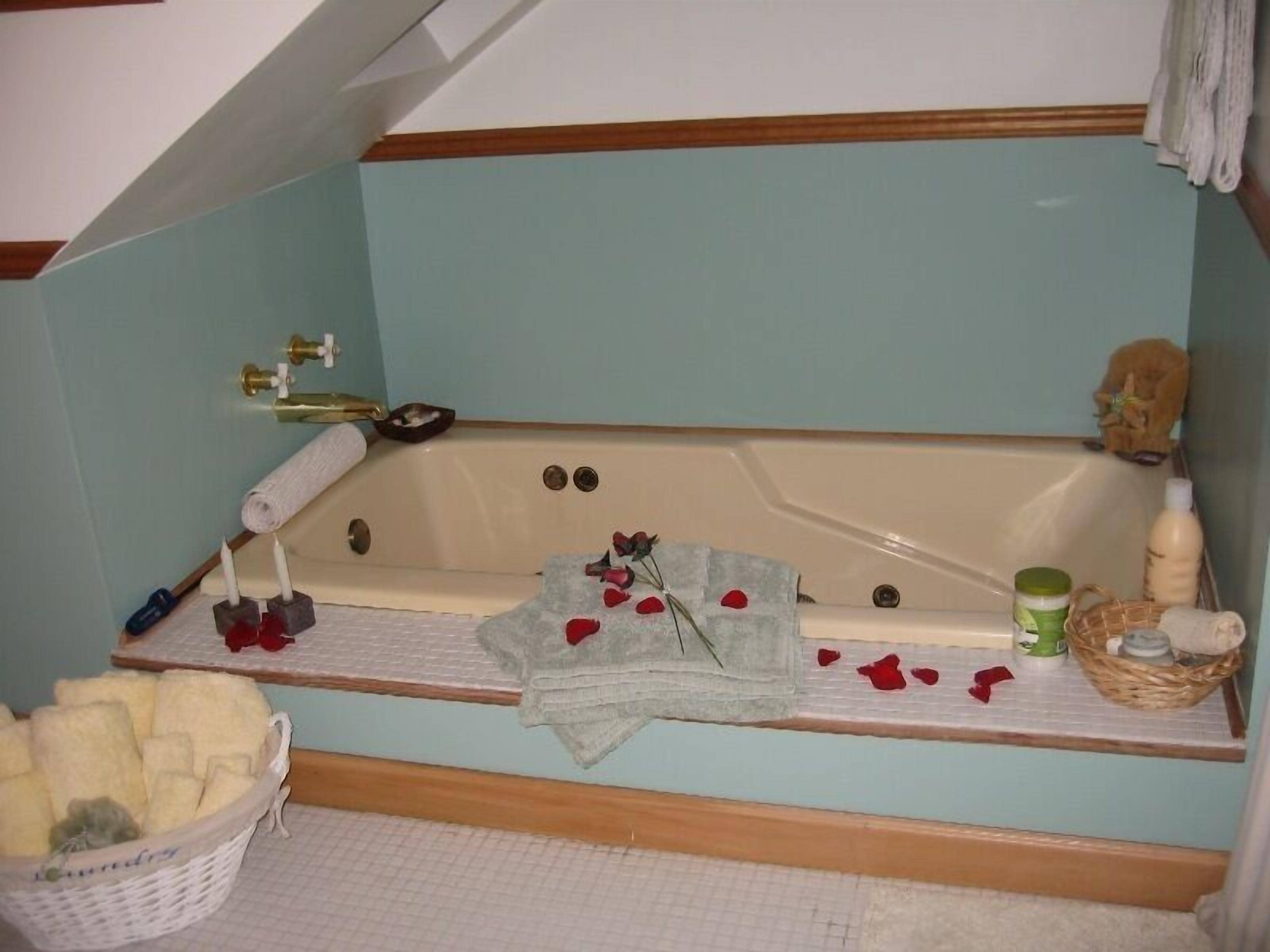 Casa de banho com banheira, toalha, cesto de produtos de higiene e uma pequena estante com uma vela e uma garrafa.