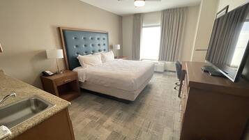 Quarto de hotel com cama, escrivaninha, cadeira, televisão, ventoinha no teto e janela com cortinas.