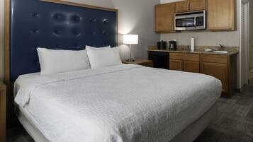 Quarto de hotel com uma cama grande, cabeceira, mesa de cabeceira, abajur, micro-ondas e cozinha compacta.