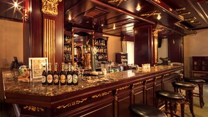 Um bar com bancada de mármore, banquetas e uma estante bem abastecida com garrafas.