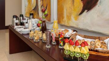 Uma mesa de buffet com diversos alimentos, incluindo frutas, doces e bebidas.