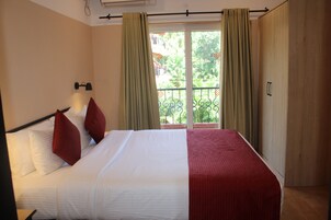 Quarto de hotel com cama, cortinas e vista para uma varanda com vegetação.