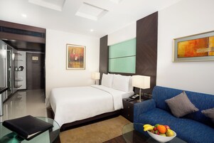 Quarto de hotel moderno com uma cama, um sofá azul, uma mesa de centro de vidro e uma fruteira.