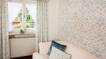 Um quarto com sofá branco, janela com cortinas e papel de parede floral.