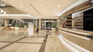 Um hall amplo com piso de mármore, um balcão de recepção e uma escadaria para os andares superiores.