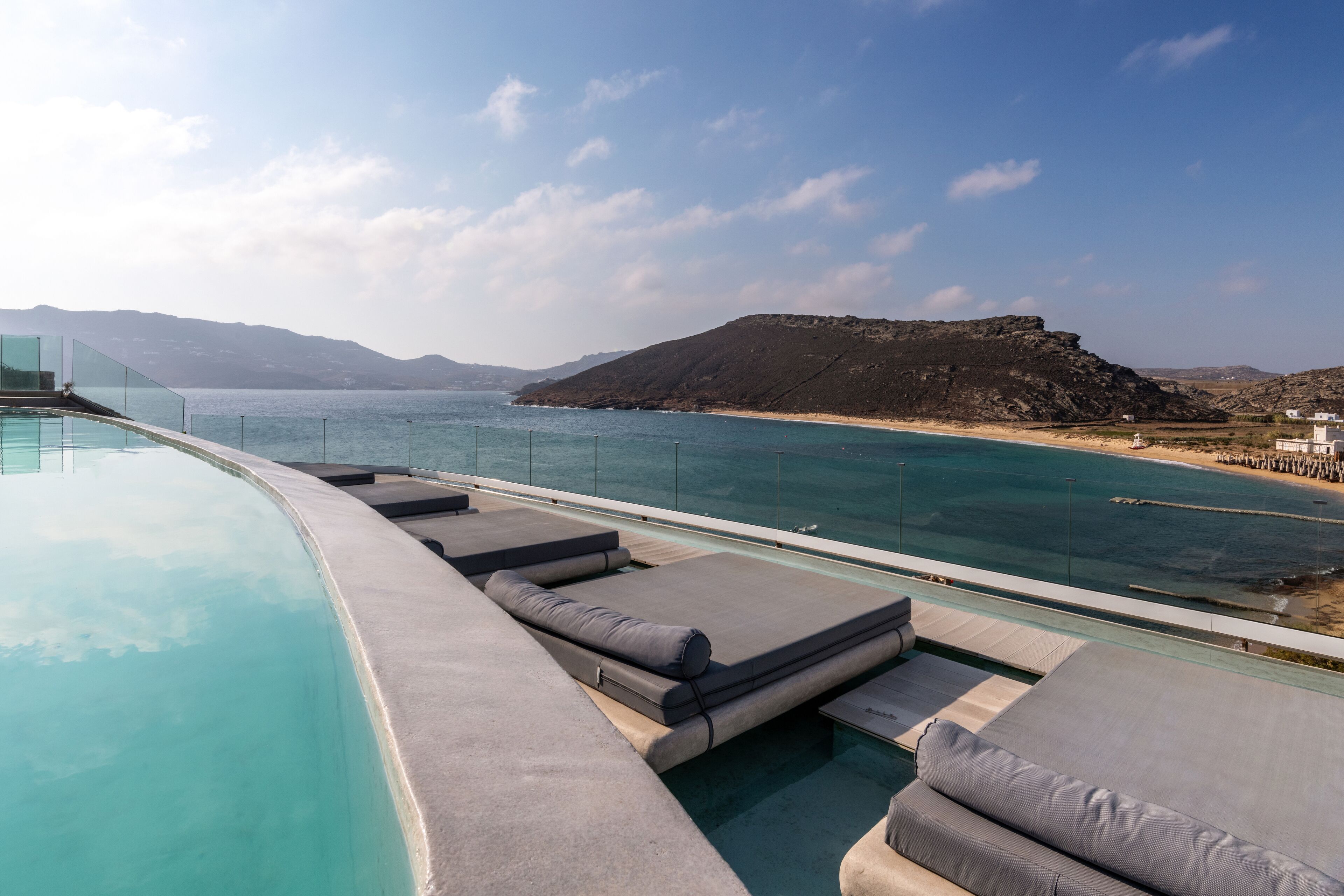 Área de piscina com espreguiçadeiras e vista para o mar e montanhas.