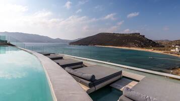 Área de piscina com espreguiçadeiras e vista para o mar e montanhas.