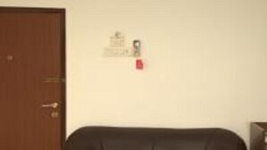 Quarto com sofá de couro marrom, porta de madeira e um pequeno quadro de avisos na parede.