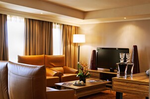 Quarto de hotel com sofá de couro, televisão de tela plana, mesa de centro de madeira e abajur.