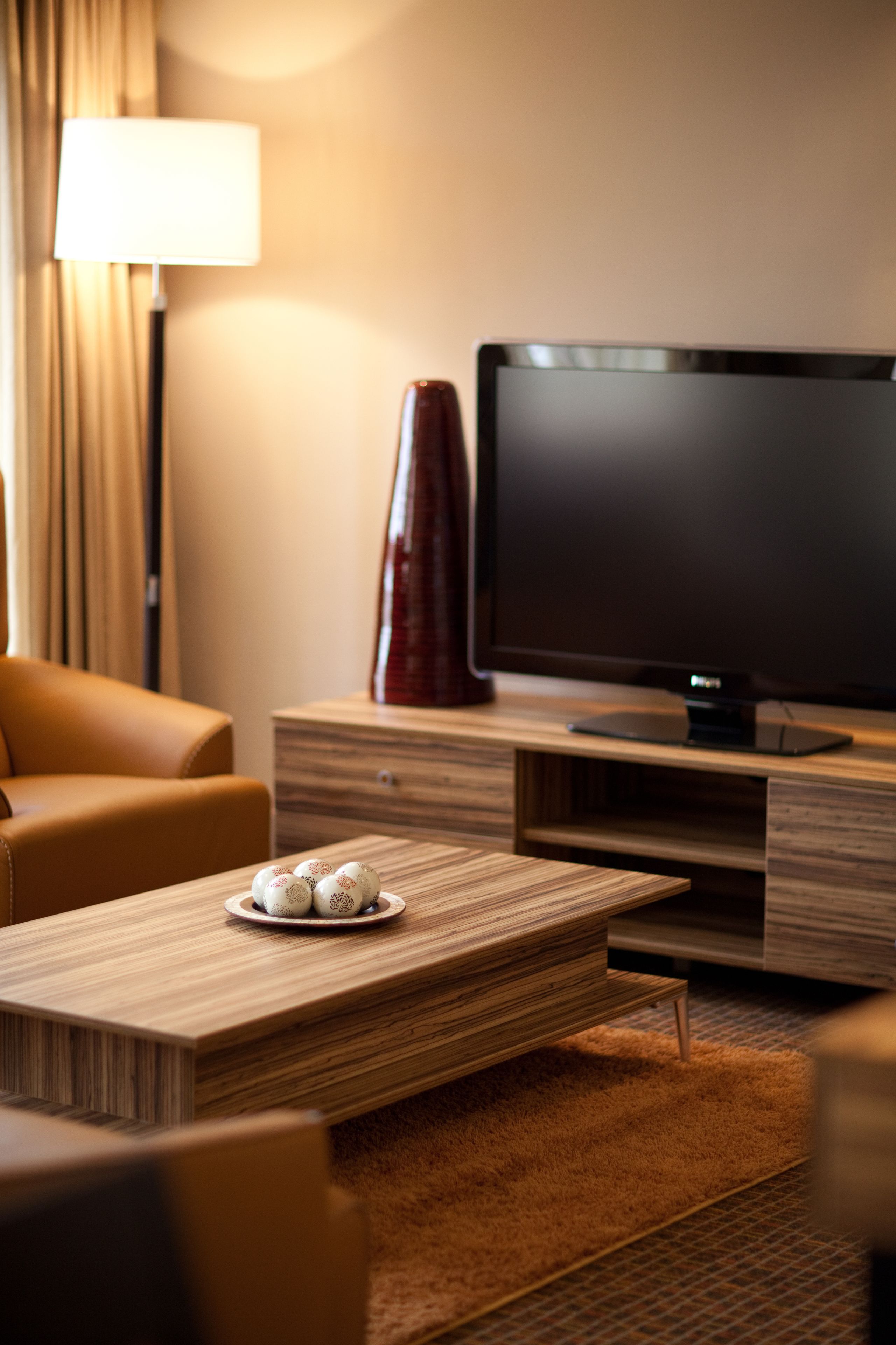 Quarto de hotel moderno com mesa de centro de madeira, TV de tela plana, sofá de couro e luminária.