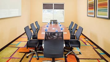 Uma sala de conferências com uma mesa comprida, cadeiras pretas e uma tela de projetor.