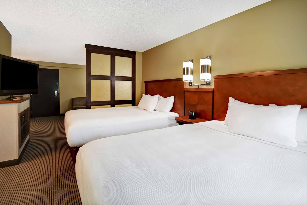 Quarto de hotel com duas camas, televisão, escrivaninha e espelho.