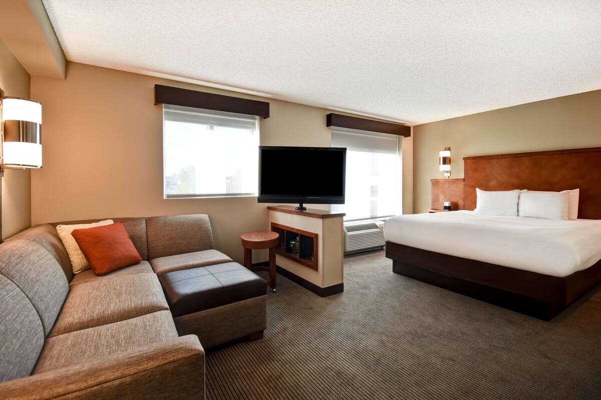 Quarto de hotel com uma cama grande, um sofá, uma televisão e uma pequena mesa.