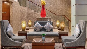 Um hall com sofá, duas poltronas, uma mesa de centro e um vaso vermelho com flores.