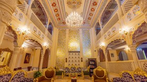 Um interior luxuoso, com lustres elaborados, mobiliário com molduras douradas e detalhes intrincados nas paredes.
