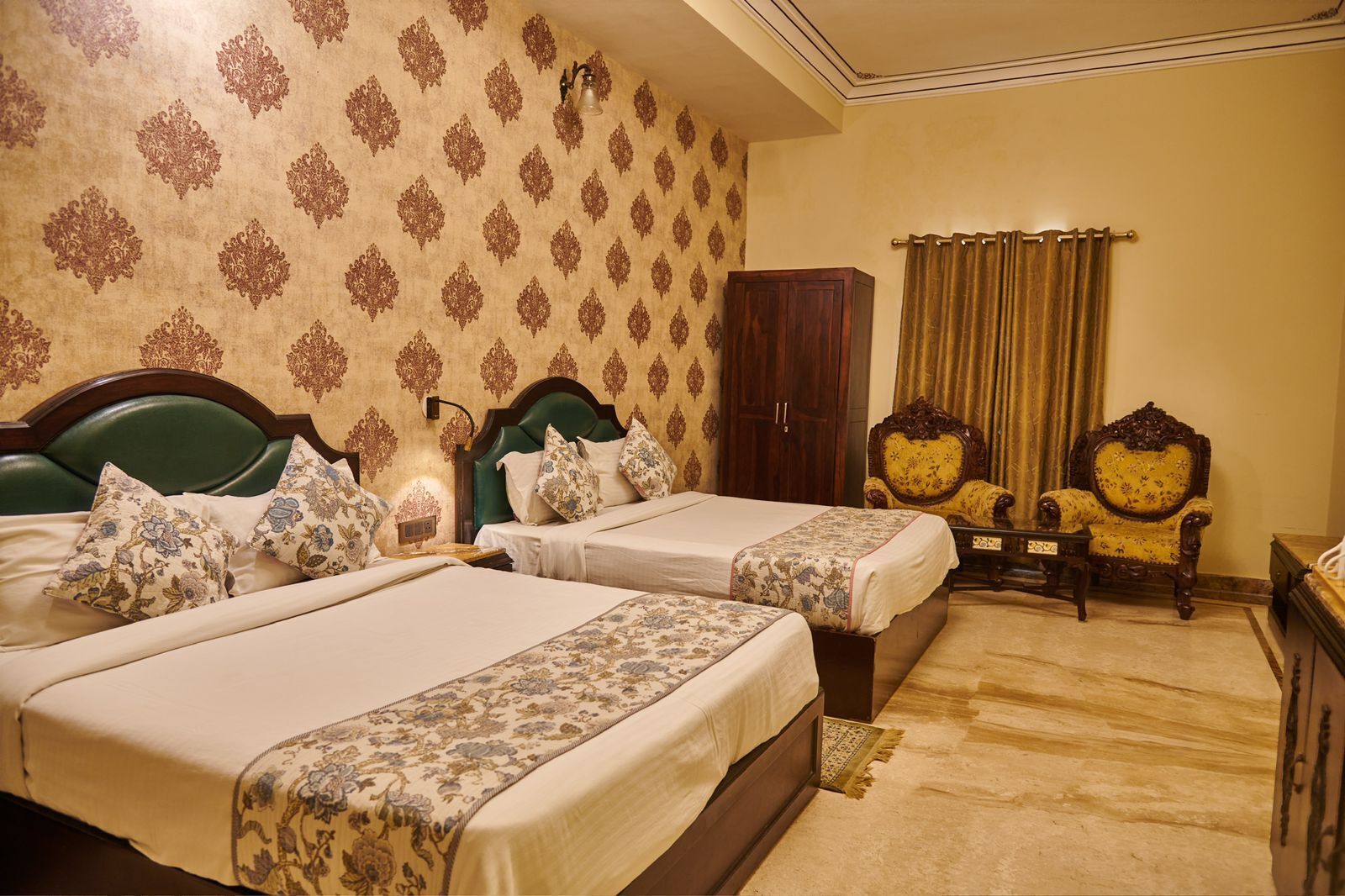 Quarto de hotel com duas camas, um guarda-roupa, duas cadeiras decoradas e uma cortina.