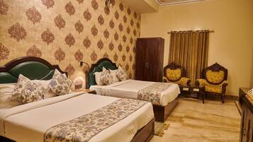 Quarto de hotel com duas camas, um guarda-roupa, duas cadeiras decoradas e uma cortina.