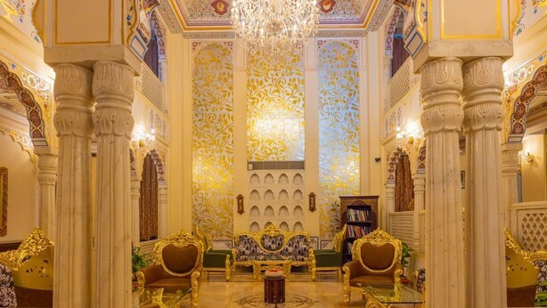 Um interior opulento com colunas ricamente decoradas, um candelabro e paredes suntuosas.