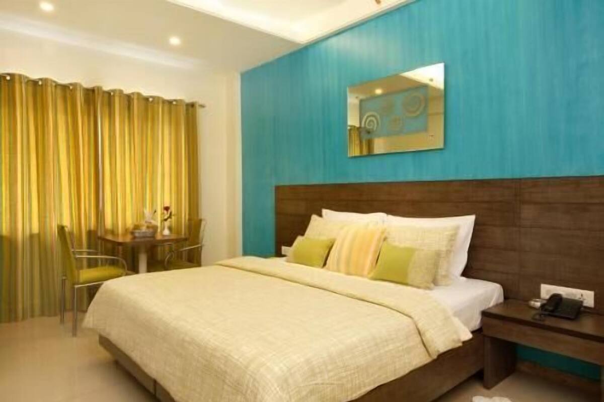 Quarto de hotel com cama, mesa de cabeceira, cadeira e espelho na parede.