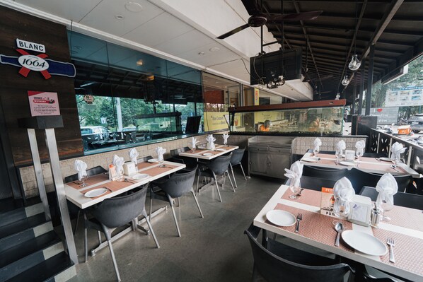Interior de restaurante com mesas postas para refeição, vista pela janela e placa com o nome do estabelecimento.