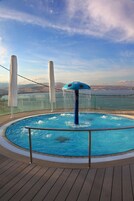 Piscina com recurso de água, rodeada por um deck de madeira e guarda-corpos de vidro, com vista para uma paisagem deslumbrante.