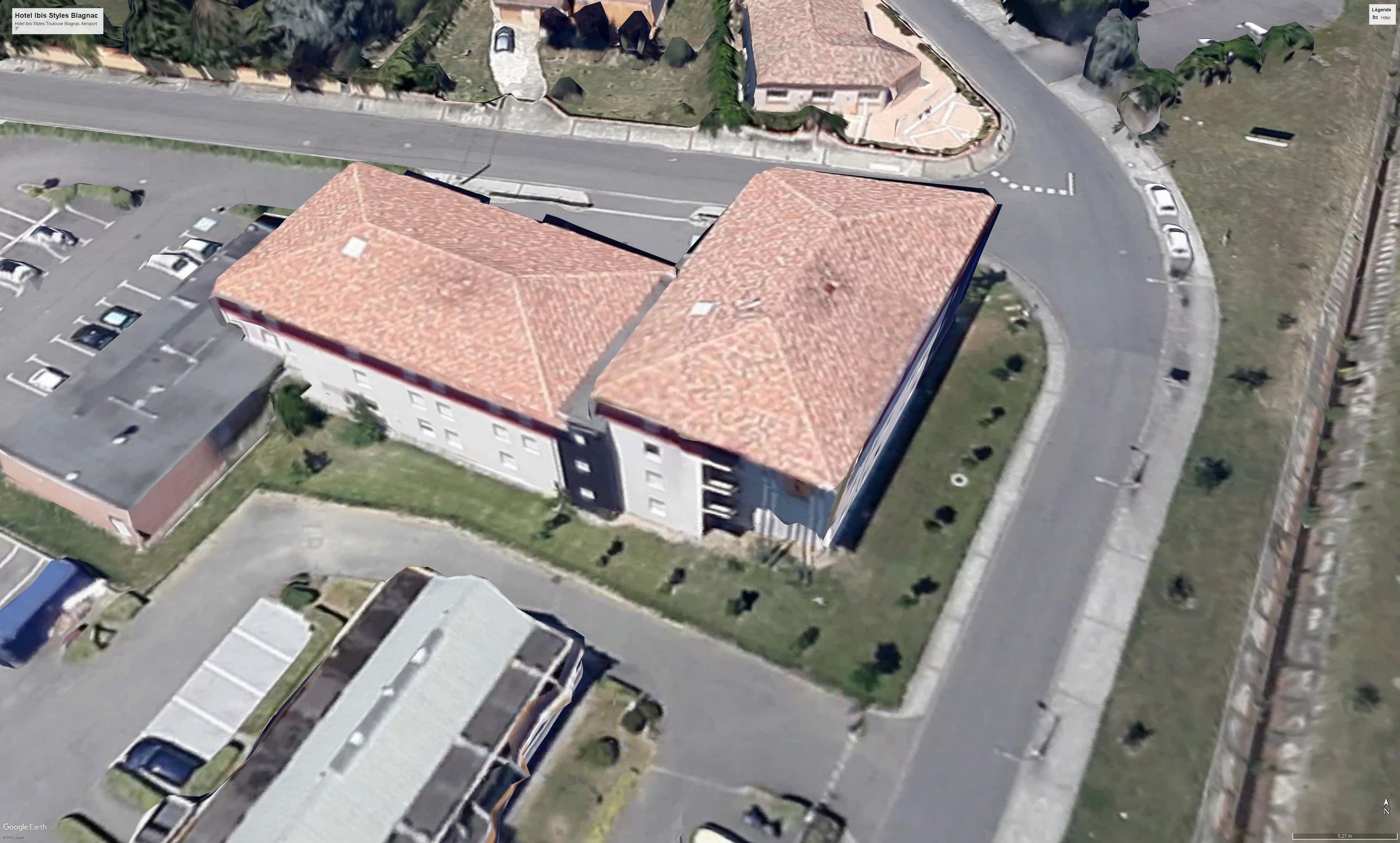 Um edifício de dois andares com telhado de telhas vermelhas, ao lado de uma estrada com carros estacionados.