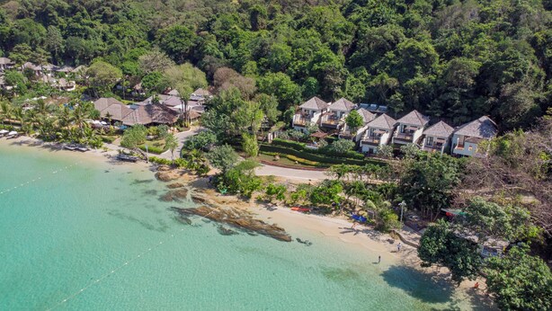 Vista aérea de um resort costeiro com várias casas no estilo de bangalô, uma praia de areia e águas turquesa cristalinas.