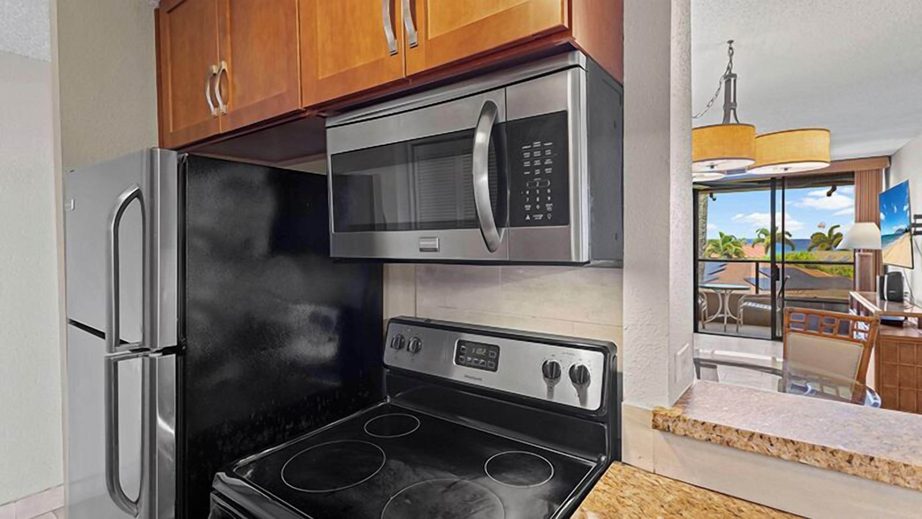 Cozinha moderna com eletrodomésticos de aço inoxidável, incluindo micro-ondas e fogão, e vista para o espaço externo da varanda.