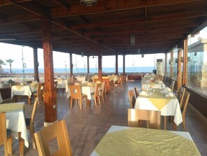Restaurante ao ar livre com mesas e cadeiras, com vista para a praia.