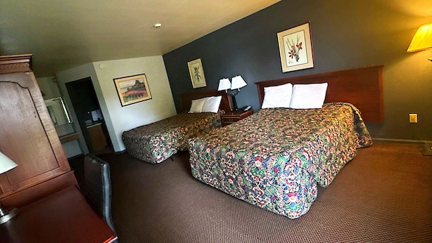 Quarto de hotel com duas camas, cabeceira de madeira, escrivaninha e uma cadeira.