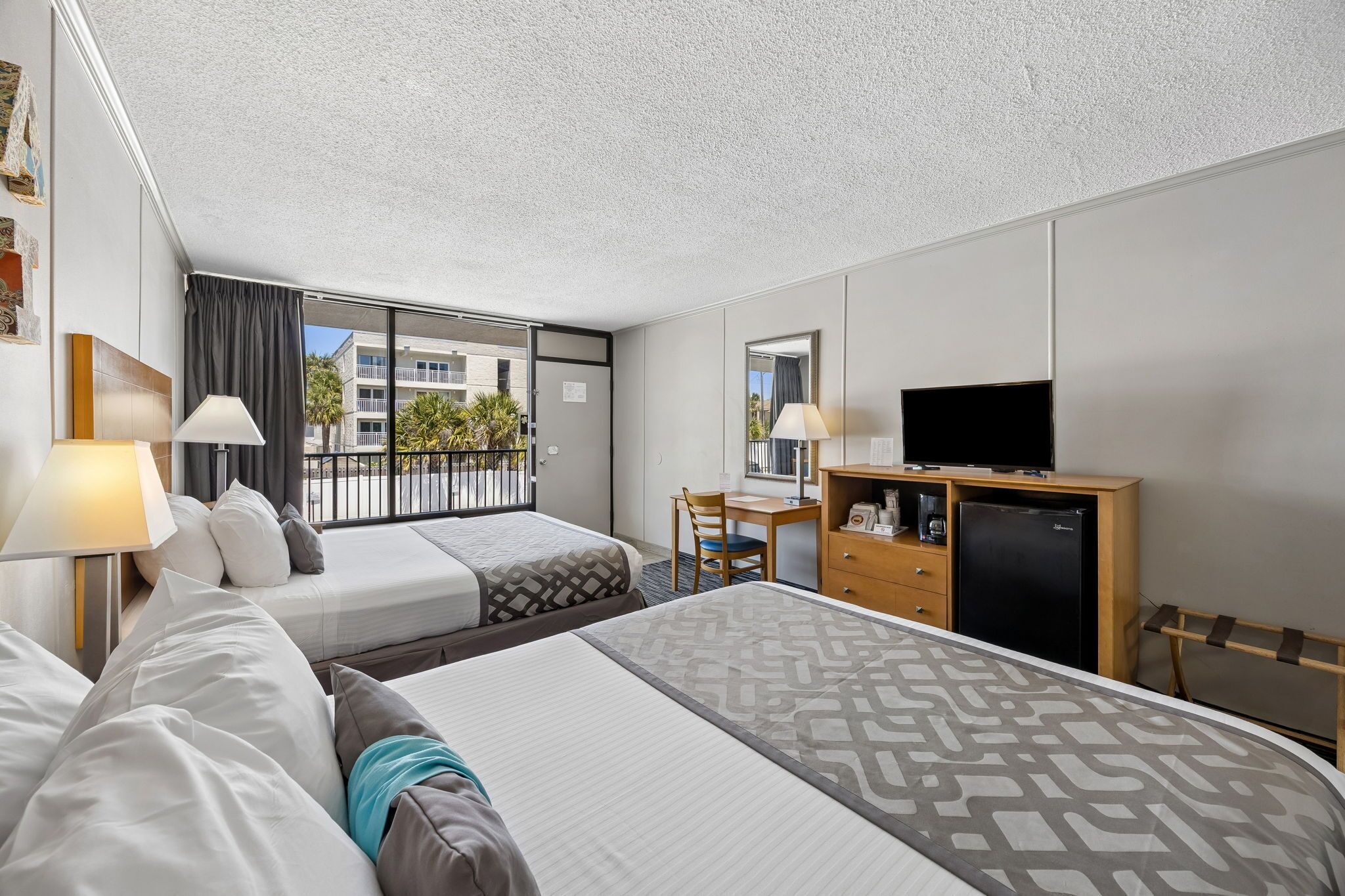 Quarto de hotel com duas camas, uma escrivaninha, televisão e frigorífico.