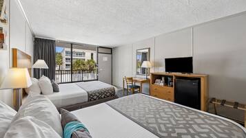 Quarto de hotel com duas camas, uma escrivaninha, televisão e frigorífico.