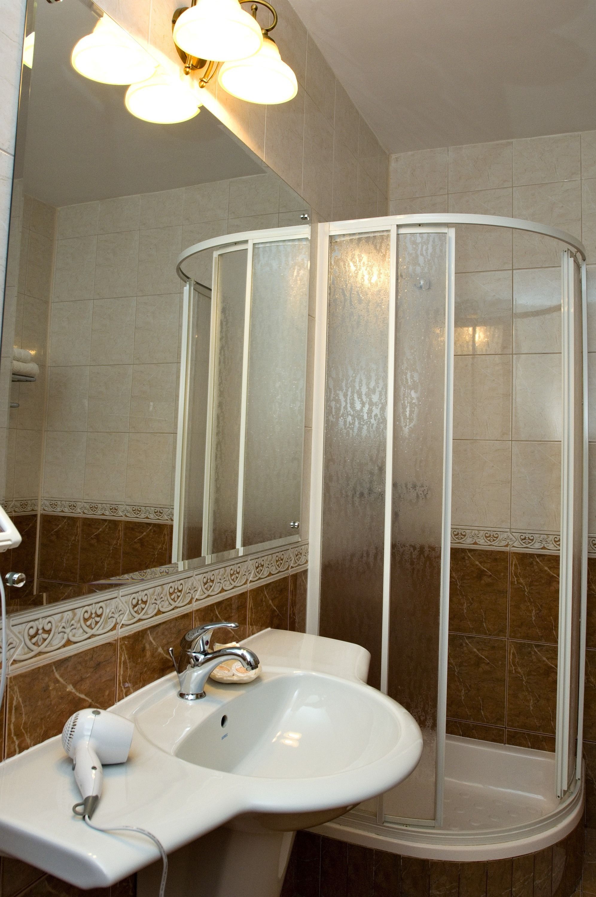 Casa de banho com chuveiro de cabine curva, lavatório com secador de cabelo e espelho com azulejos decorativos.