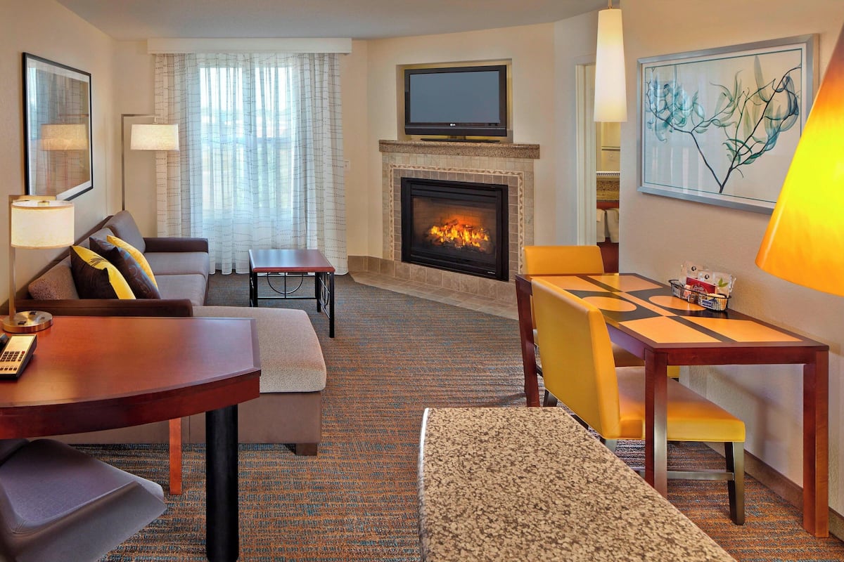 Quarto de hotel com lareira, sofá, mesa de jantar e televisão montada acima da lareira.