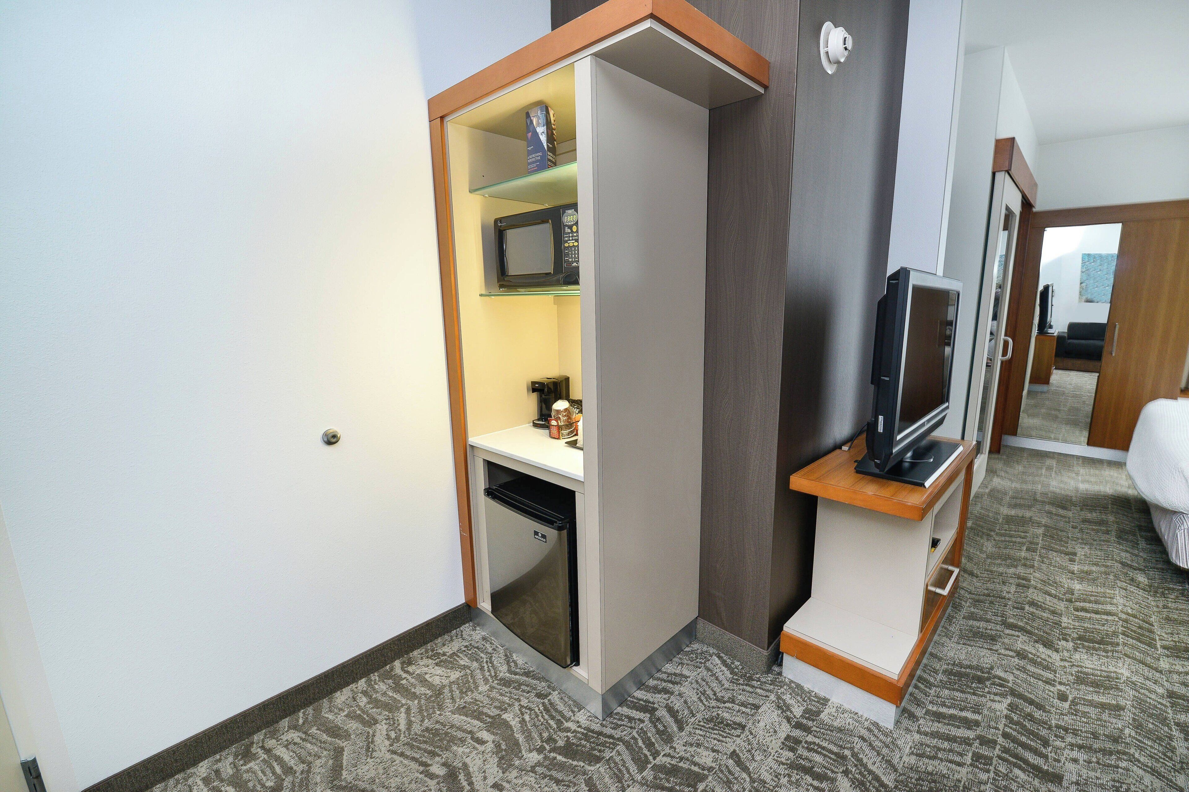 Quarto de hotel compacto com cozinha compacta, televisão e uma pequena área de estar.