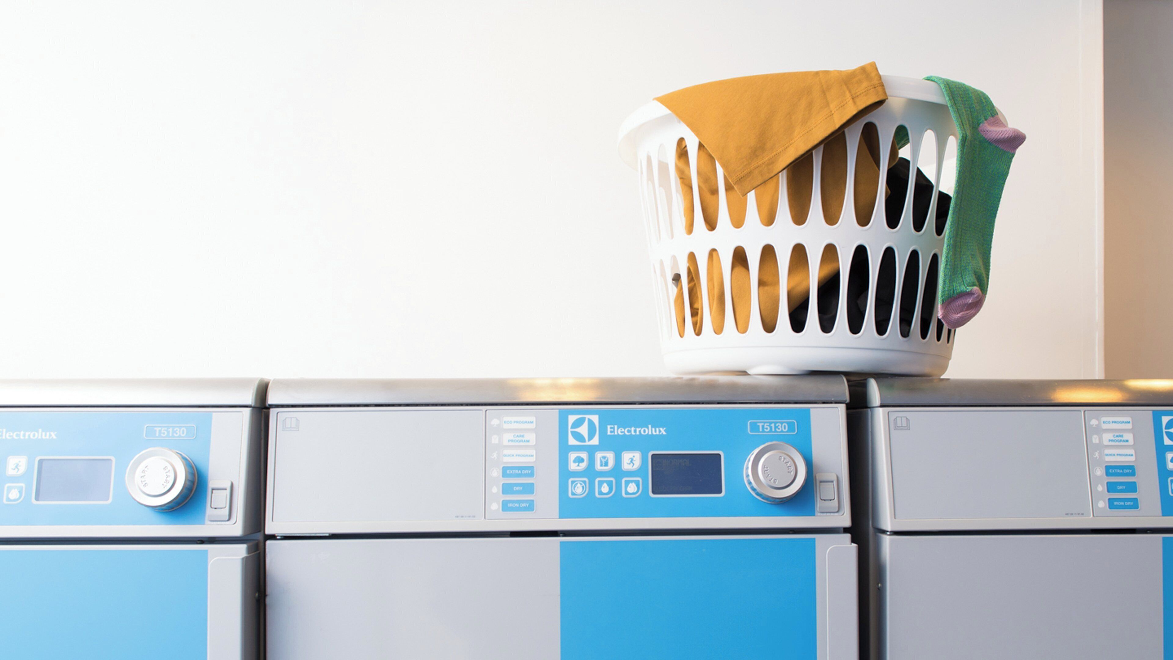 Cesto de roupa com uma toalha em cima de uma fileira de máquinas de lavar Electrolux.