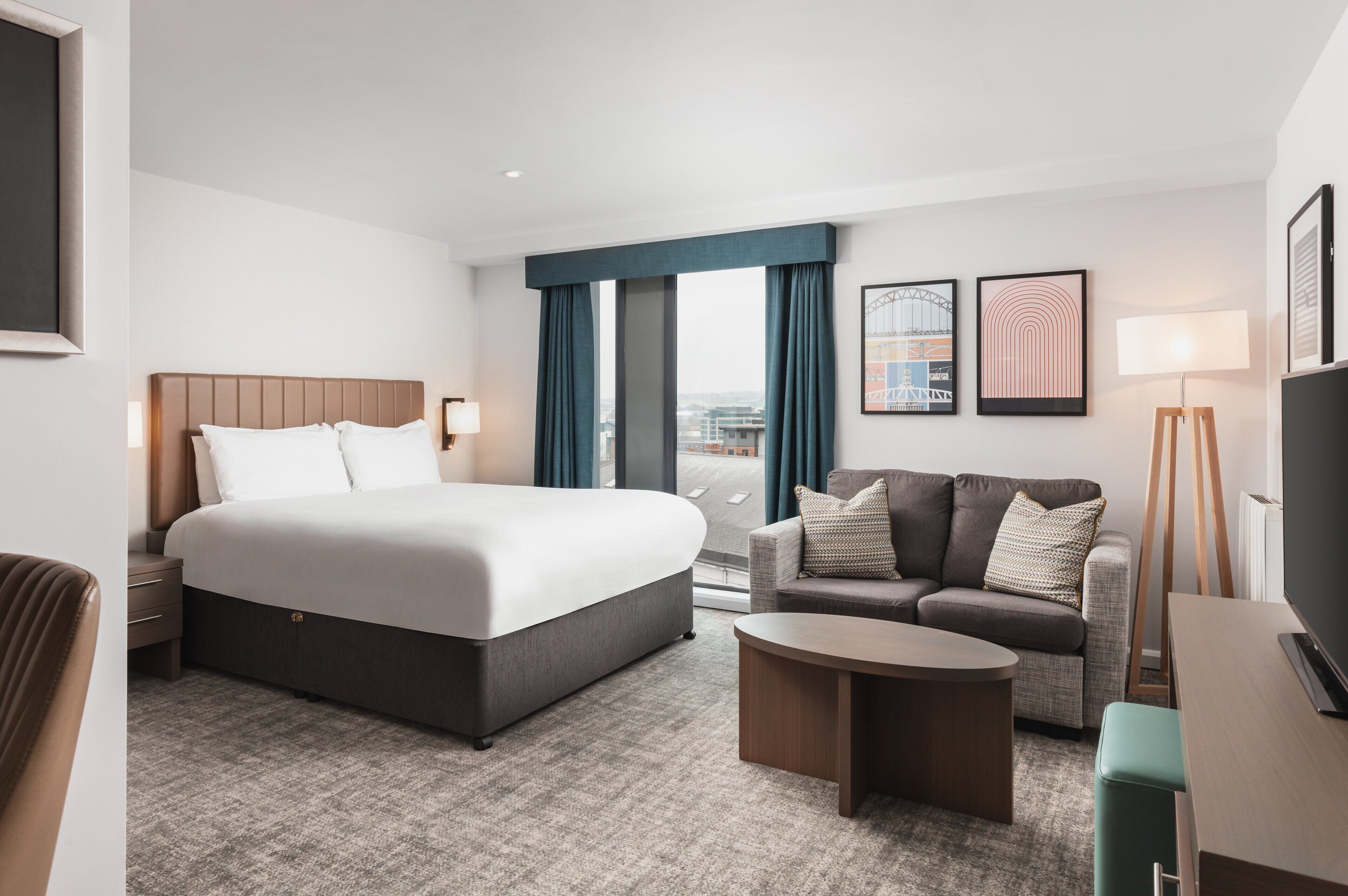 Quarto de hotel com uma cama grande, um sofá, uma mesa de centro e uma televisão.