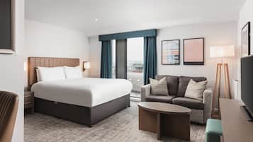 Quarto de hotel com uma cama grande, um sofá, uma mesa de centro e uma televisão.