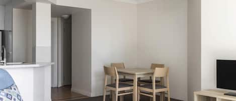 Uma sala de estar moderna com área de refeições, um sofá, uma TV em um suporte e uma cozinha ao fundo.