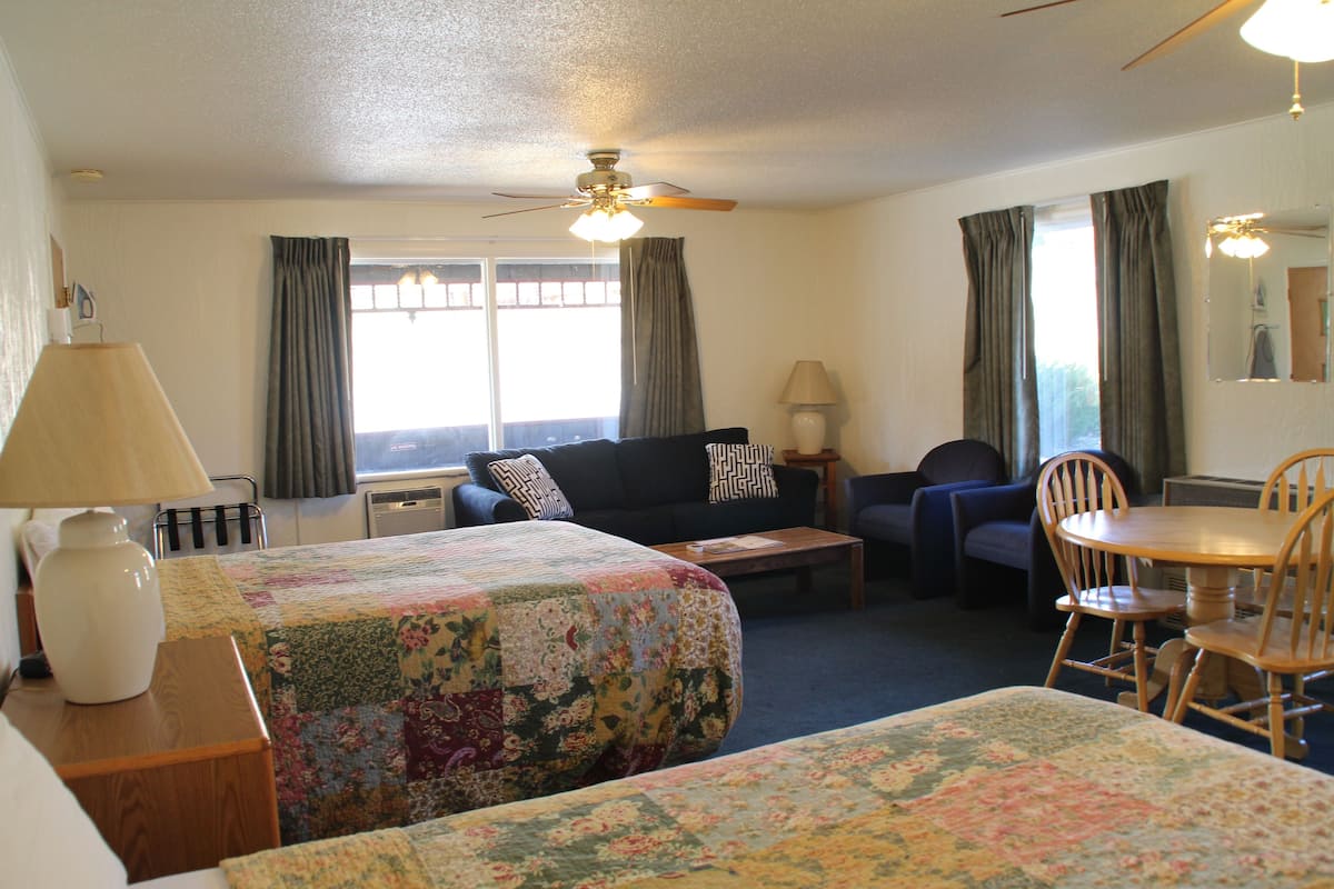Quarto de hotel com duas camas, um sofá, uma mesa de jantar e um ventilador de teto.